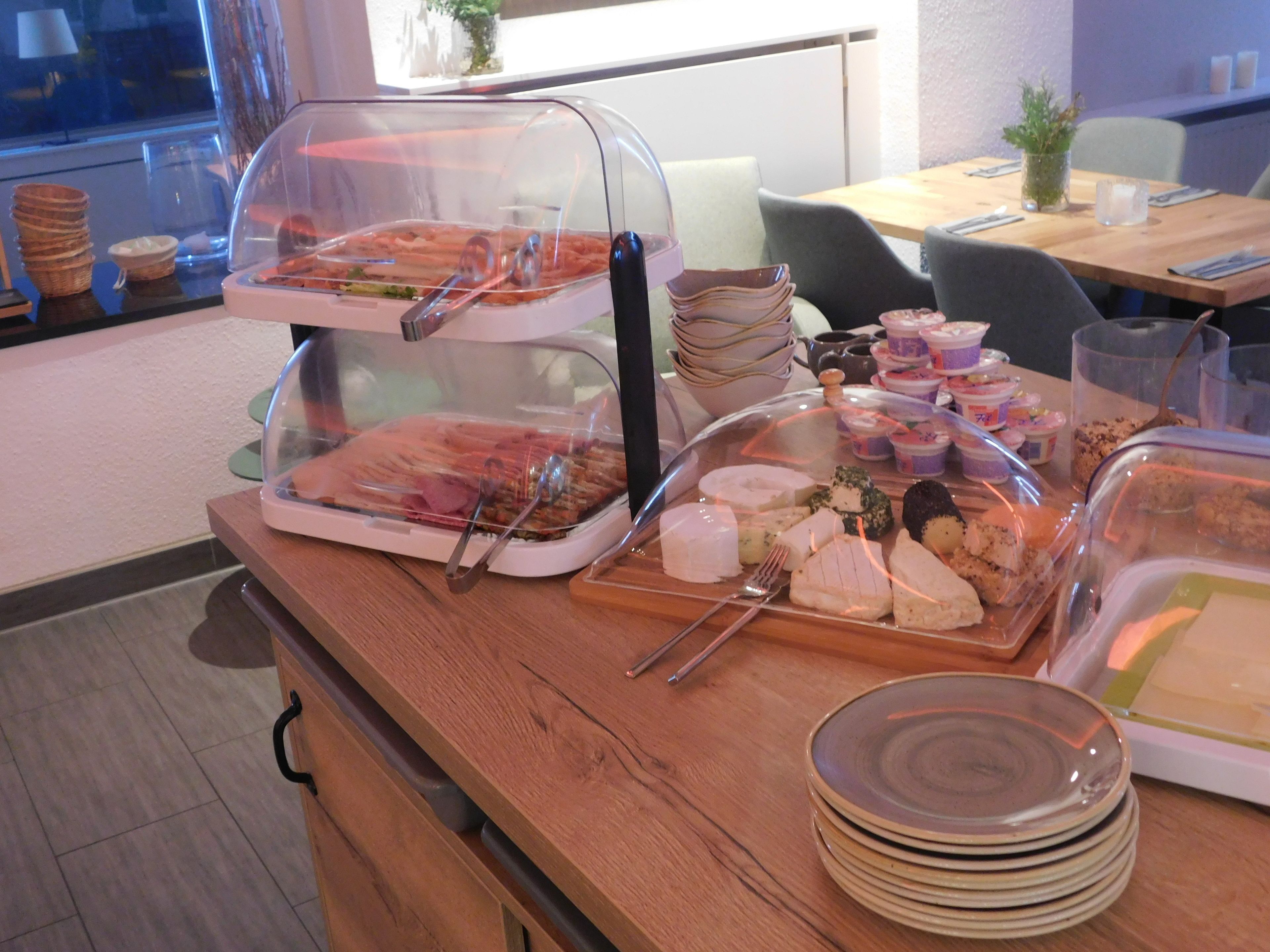 Disposição de buffet com pratos de servir tampados e uma variedade de alimentos.