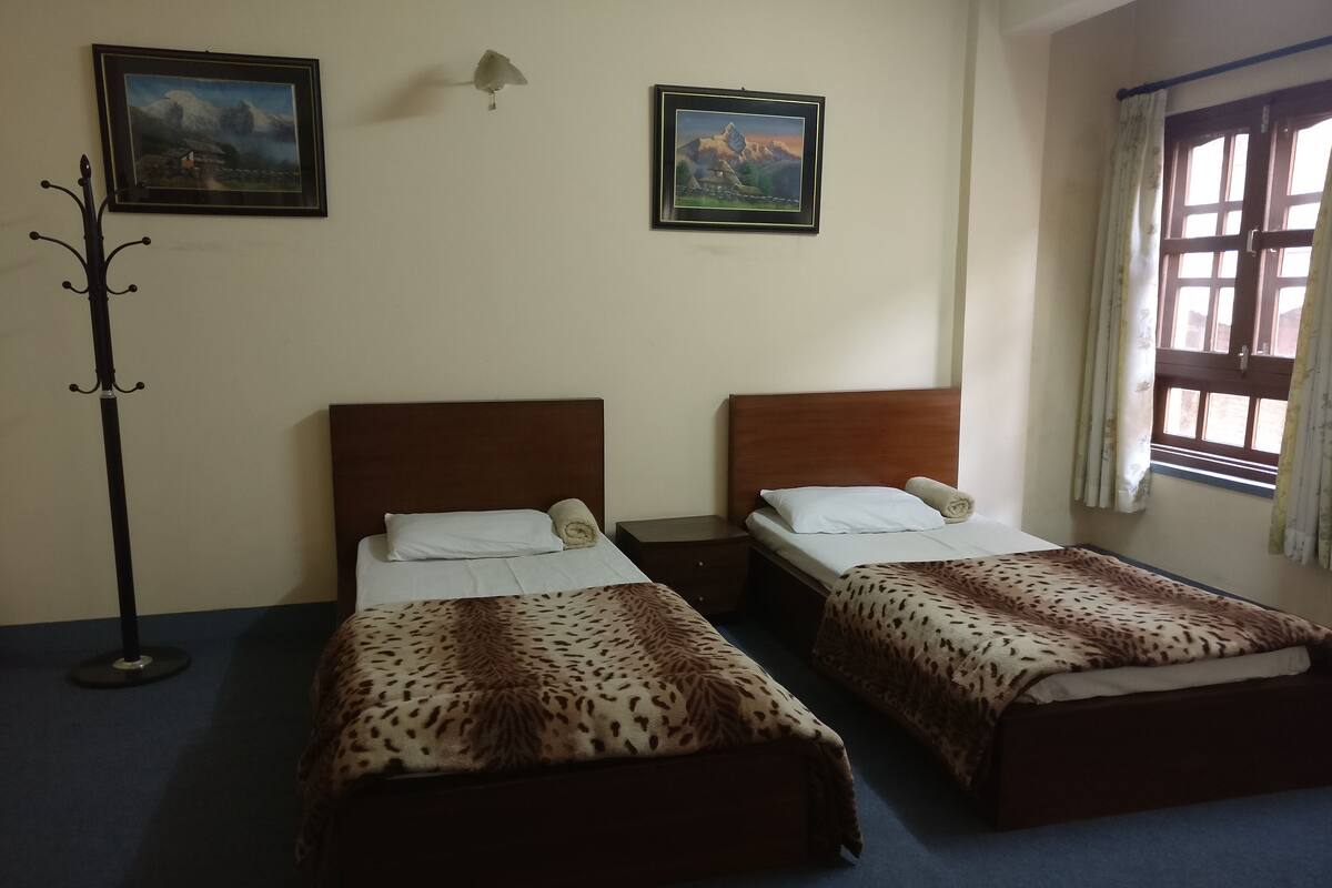 Quarto de hotel com duas camas, cada uma com colcha de estampa de leopardo, mesa de cabeceira, abajur e duas fotos emolduradas na parede.