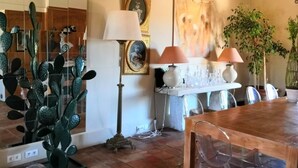 Uma área de refeições com mesa de madeira, cadeiras transparentes, uma escultura de cacto e um espelho refletindo o espaço.