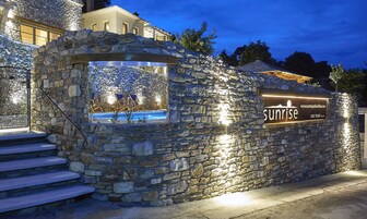 Um muro de pedra com piscina e espreguiçadeiras, uma escadaria e um letreiro para Sunrise Pelican Villas.