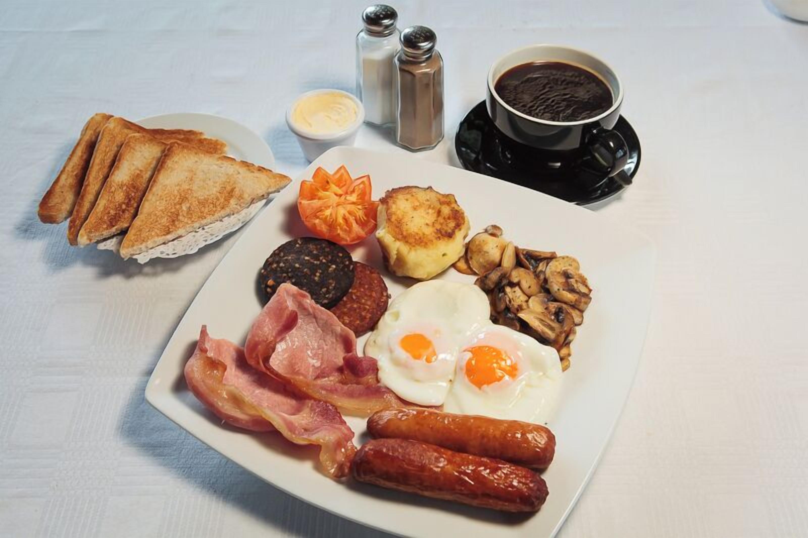 Prato de pequeno-almoço com torradas, ovos, salsichas, bacon, cogumelos e uma chávena de café.