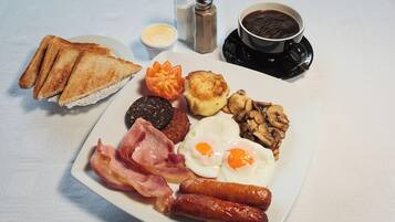 Prato de pequeno-almoço com torradas, ovos, salsichas, bacon, cogumelos e uma chávena de café.