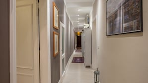 Um corredor com quadros nas paredes, um tapete estampado no chão e um candeeiro do lado direito.
