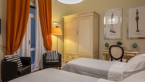 Quarto de hotel com duas camas, uma escrivaninha, uma cadeira, um guarda-roupa e um abajur.