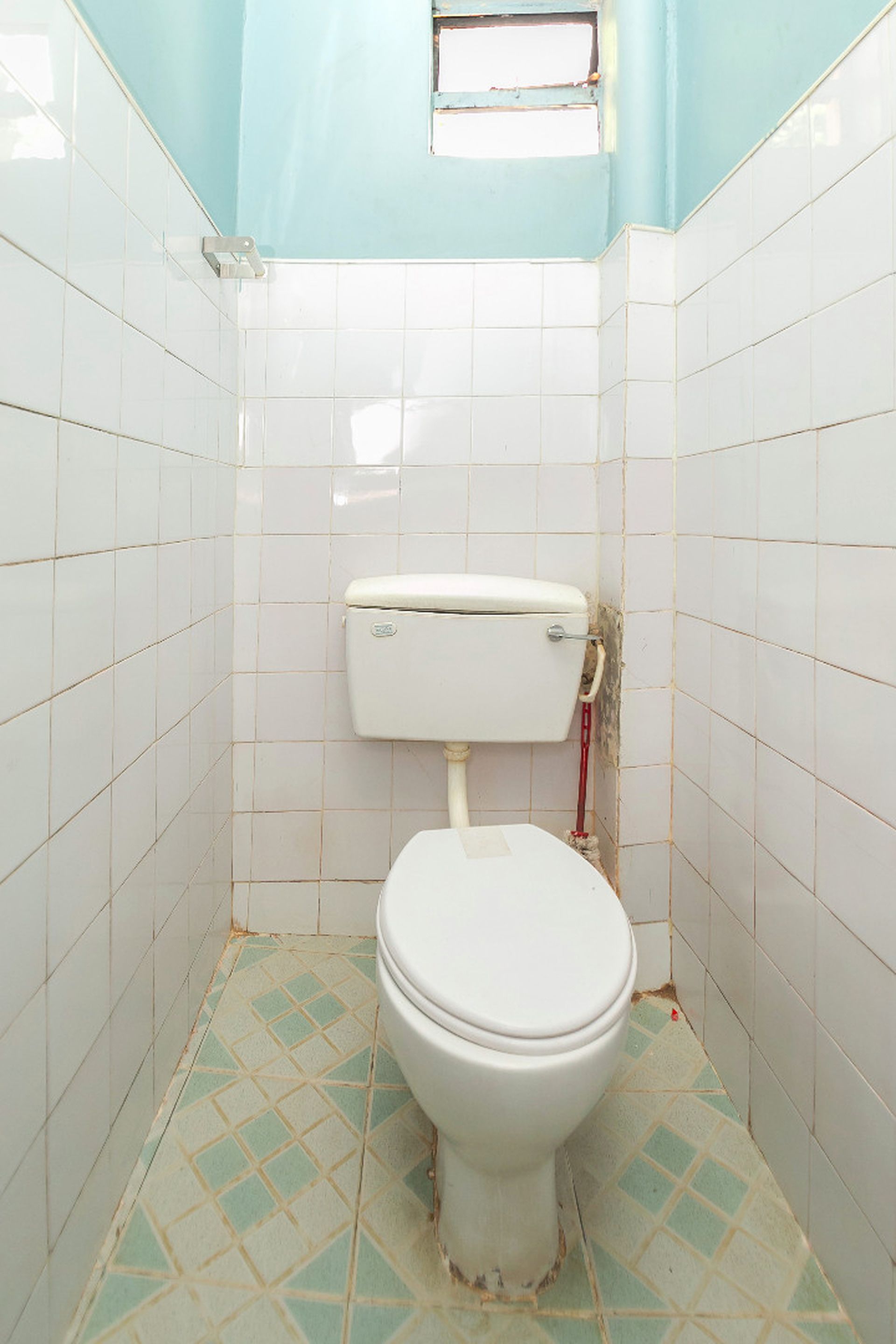 Um banheiro pequeno revestido com azulejos, com vaso sanitário, janela e uma parede danificada.