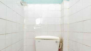 Um banheiro pequeno revestido com azulejos, com vaso sanitário, janela e uma parede danificada.