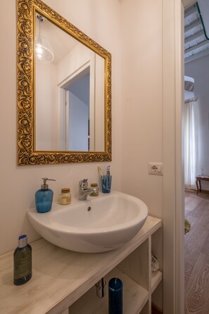 Casa de banho com lavatório branco, espelho com moldura dourada e dispensador de sabonete azul.