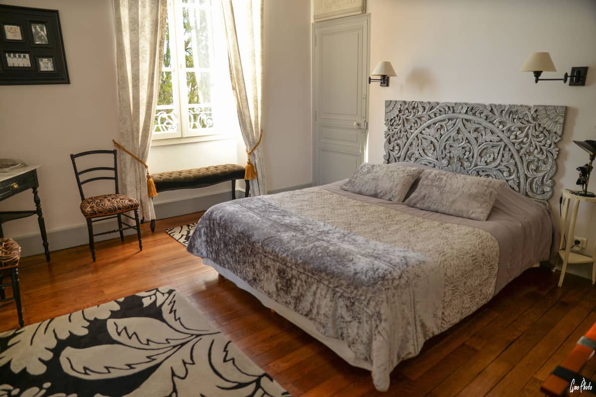 Quarto com cama, cadeira, escrivaninha e janela com cortinas.