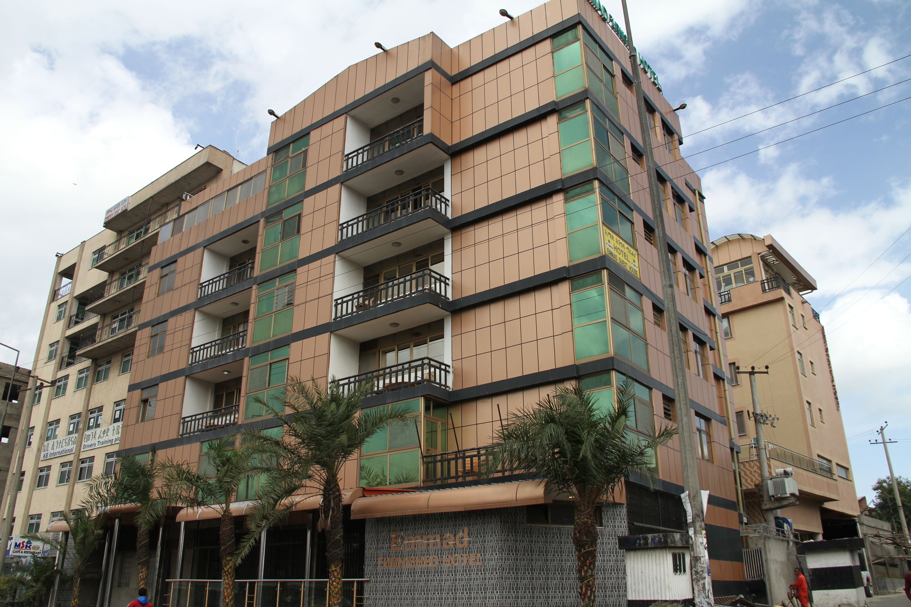 Um hotel de vários andares com varandas, fachada de pedra e palmeiras na frente.