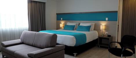 Quarto de hotel moderno com uma cama grande, um sofá, uma escrivaninha e uma cadeira.