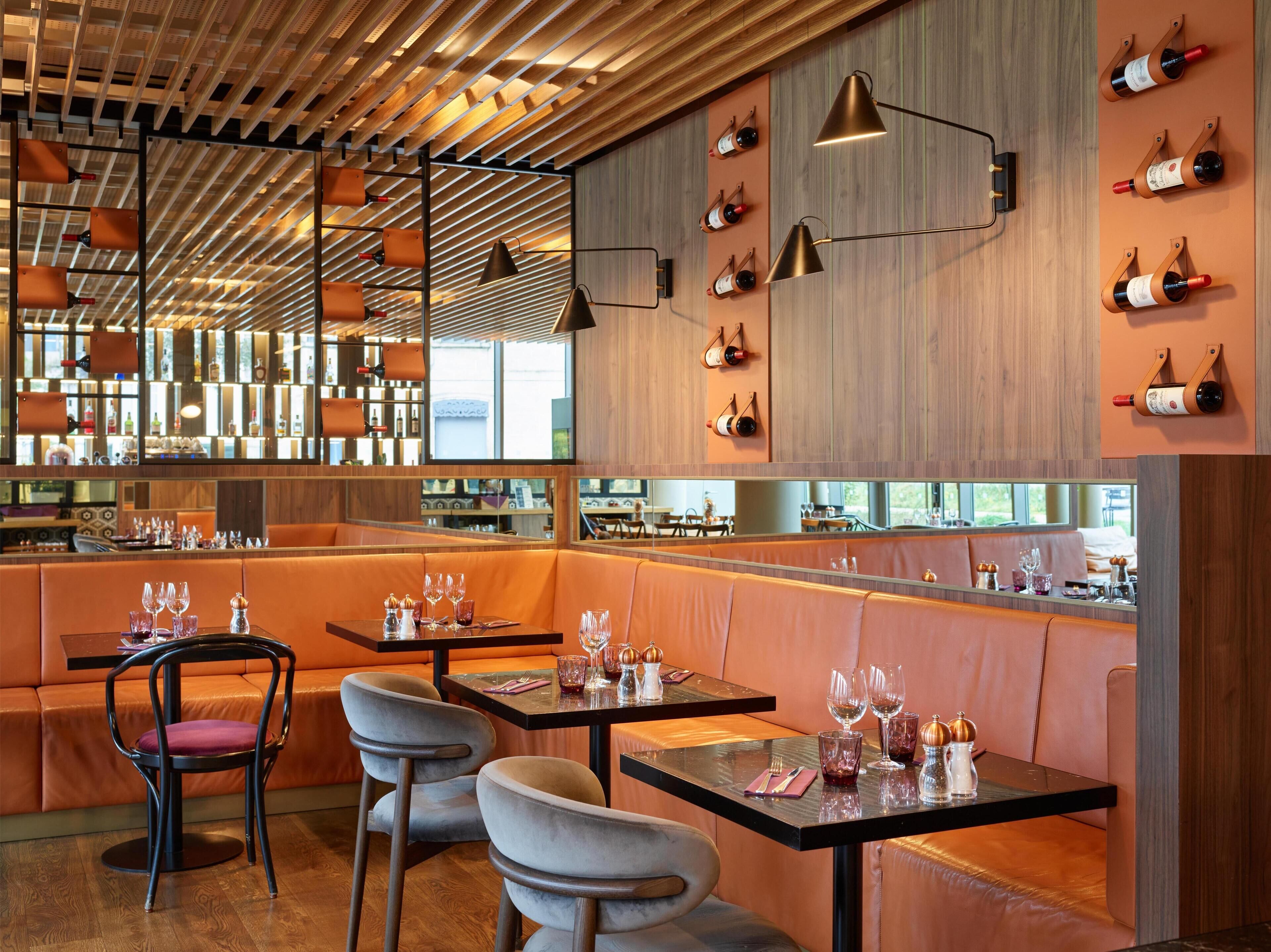 Interior de restaurante moderno com teto de madeira, assentos de couro e garrafas de vinho na parede.