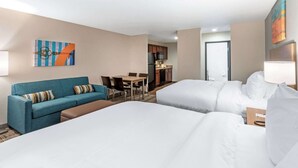 Quarto de hotel com duas camas, um sofá, uma mesa de jantar e uma cozinha.