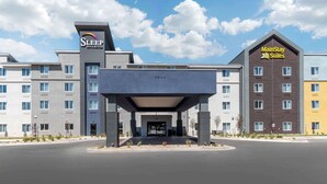 Um hotel com design moderno, apresentando uma entrada central coberta, vários andares e diversos tipos de quartos.