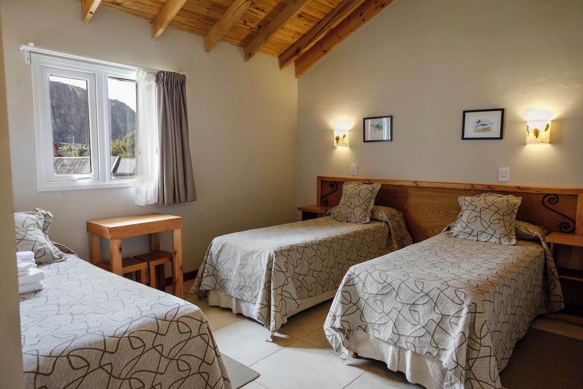 Quarto com duas camas, uma escrivaninha de madeira e uma janela com cortinas.