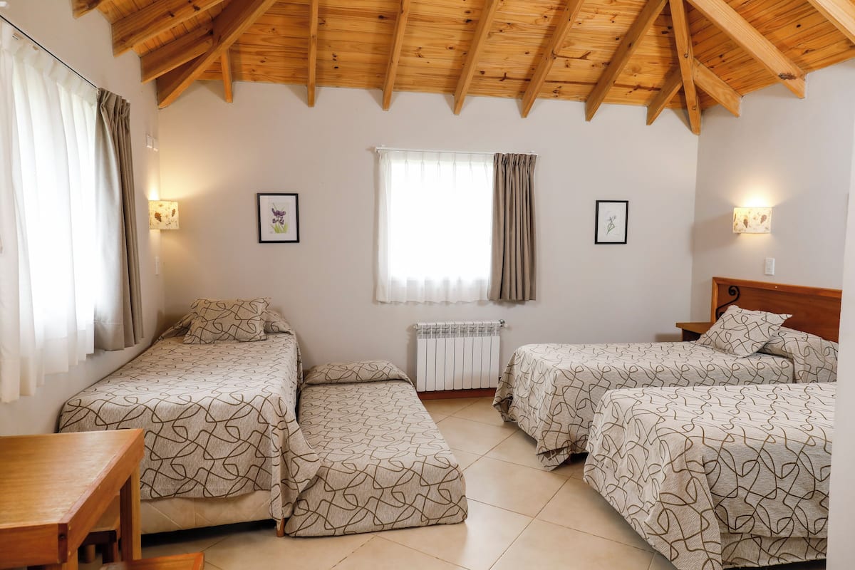 Quarto com duas camas, teto de madeira, radiador e luminárias fixadas na parede.