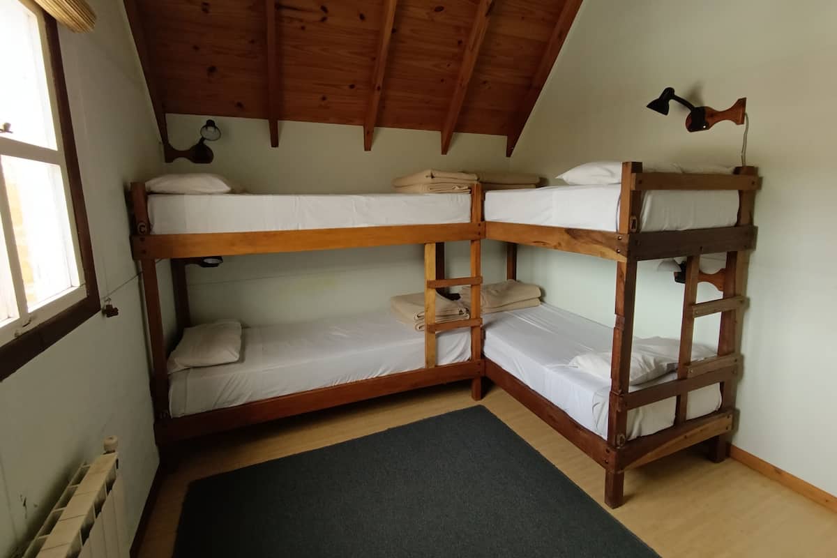 Quarto com beliches, vigas de madeira e janela.