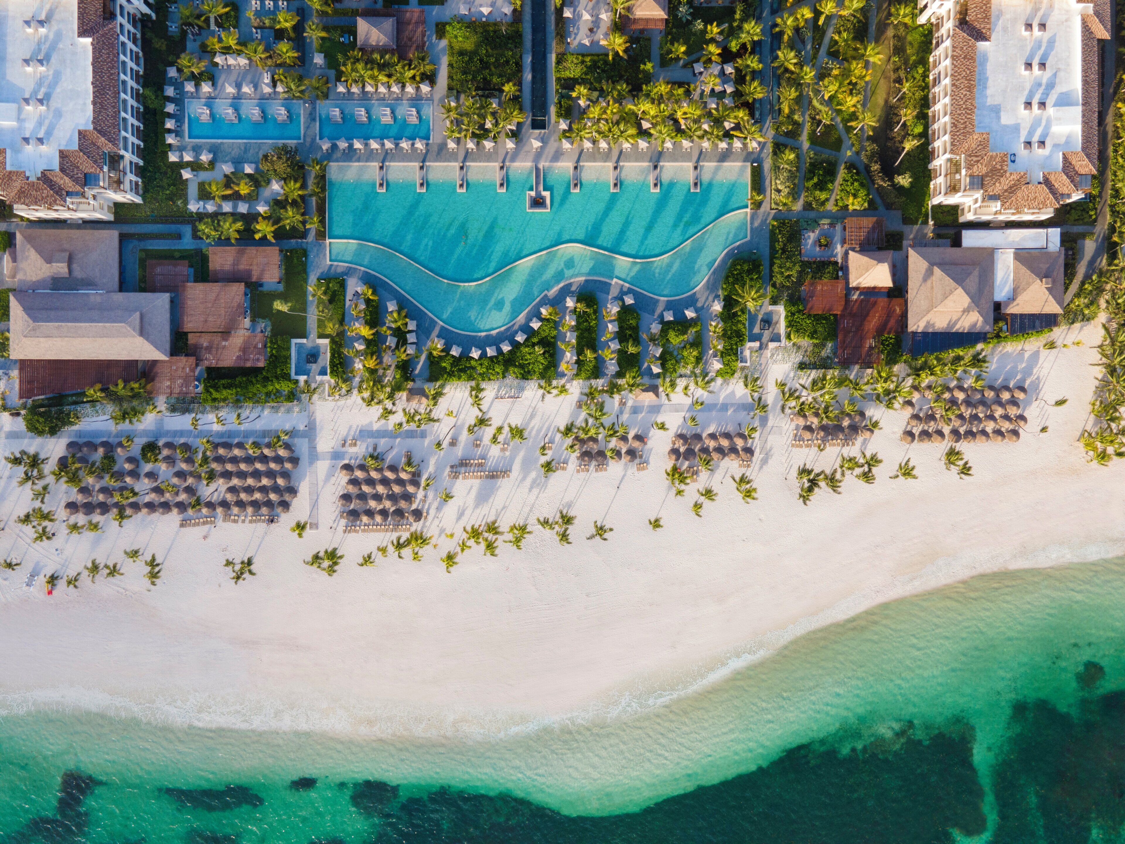 Vista aérea de um resort com uma grande piscina, área de praia e vários edifícios.