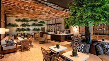 Restaurante moderno com teto de madeira, plantas de bambu e um espaço de bar central.