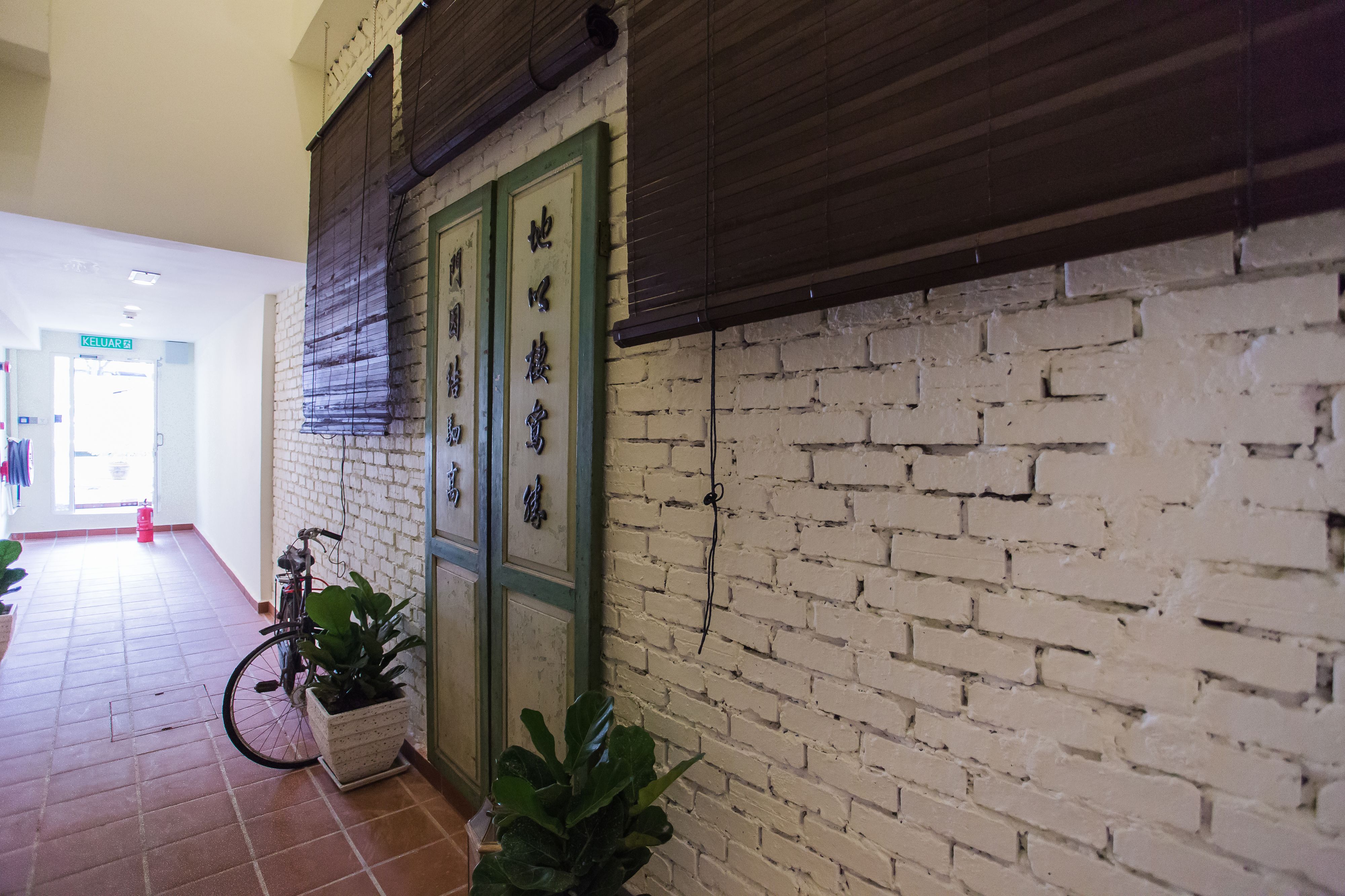 Um corredor com parede de tijolos, uma porta verde com caracteres chineses e uma bicicleta encostada na parede.