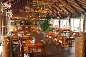 Um restaurante amplo, com mesas e cadeiras de madeira, plantas pendentes e iluminação pendente.