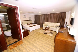 Quarto de hotel com cama, sofá, televisão e banheiro.