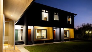 Uma casa moderna de dois andares com janelas grandes e fachada bem iluminada ao entardecer.