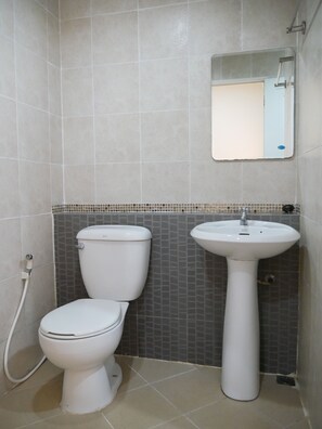 Um banheiro com vaso sanitário e pia de pedestal, ambos brancos, em frente a uma parede revestida de azulejos com borda estampada.