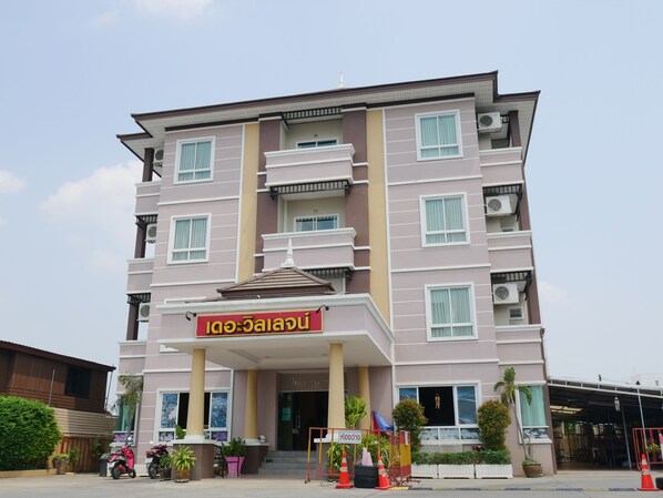 Um hotel com vários andares, entrada central, varandas e aparelhos de ar condicionado.