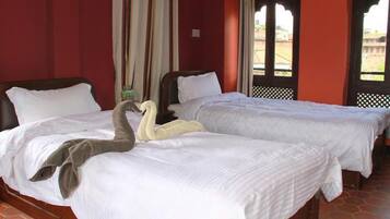 Quarto de hotel com duas camas, parede vermelha e vista exterior pela janela.