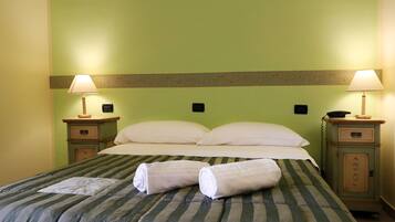 Quarto de hotel com uma cama, duas mesas de cabeceira, luminárias e um criado-mudo.