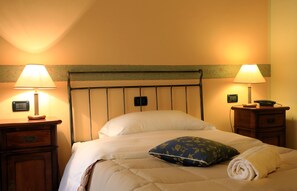 Cama bem arrumada com edredom branco e almofada floral azul, com duas mesas de cabeceira laterais, uma delas com um telefone.
