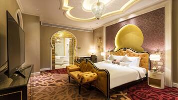 Quarto de hotel com uma cama grande, um sofá, uma televisão e uma escrivaninha.