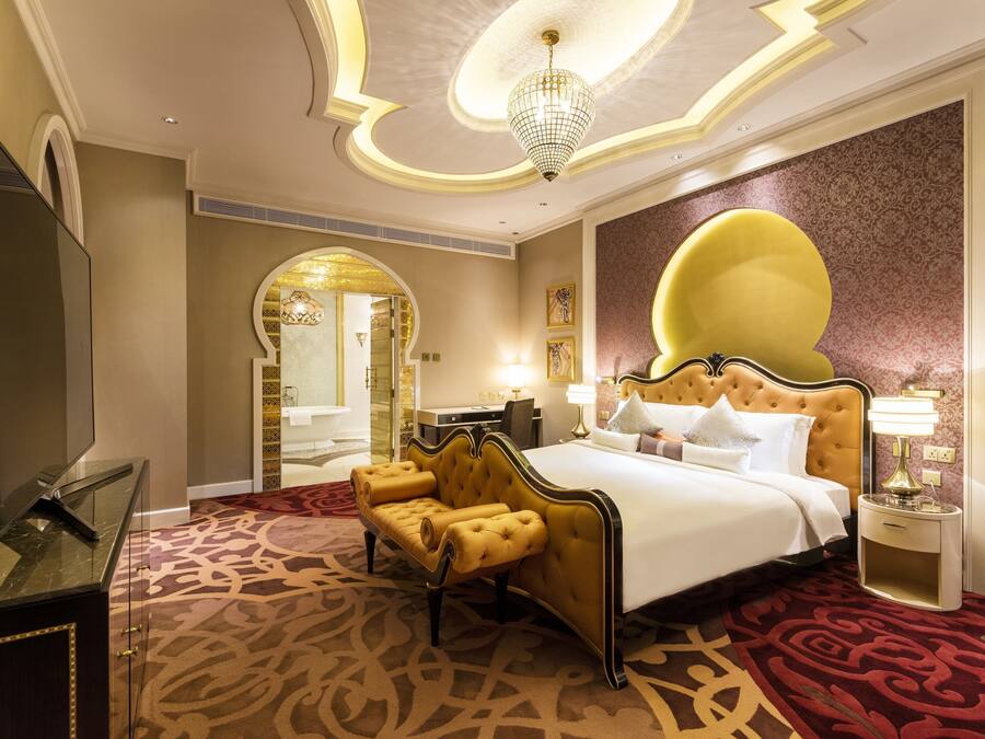 Quarto de hotel com uma cama grande, um sofá, uma televisão e uma escrivaninha.