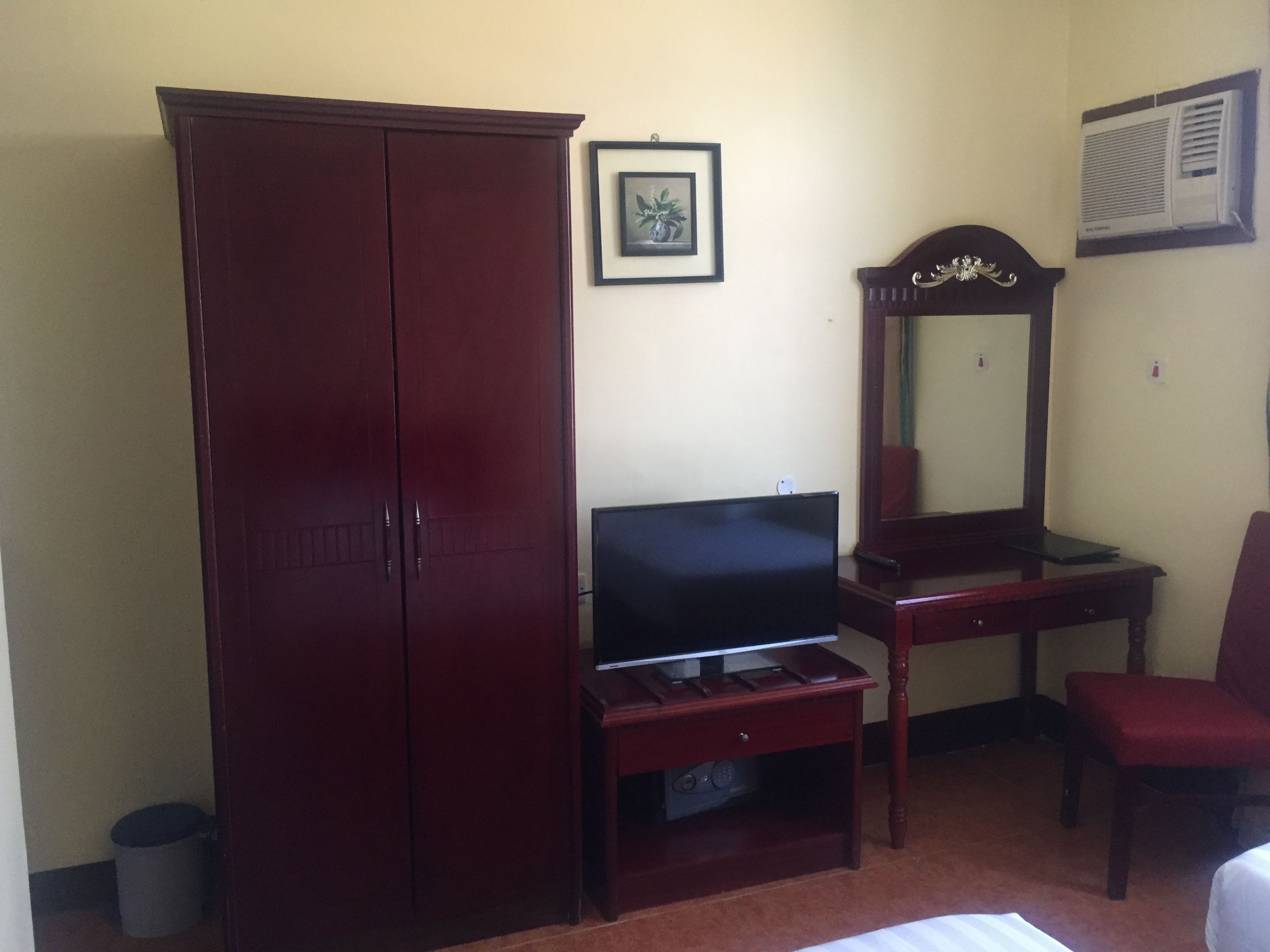 Quarto com guarda-roupa, escrivaninha, cadeira, televisão e espelho.