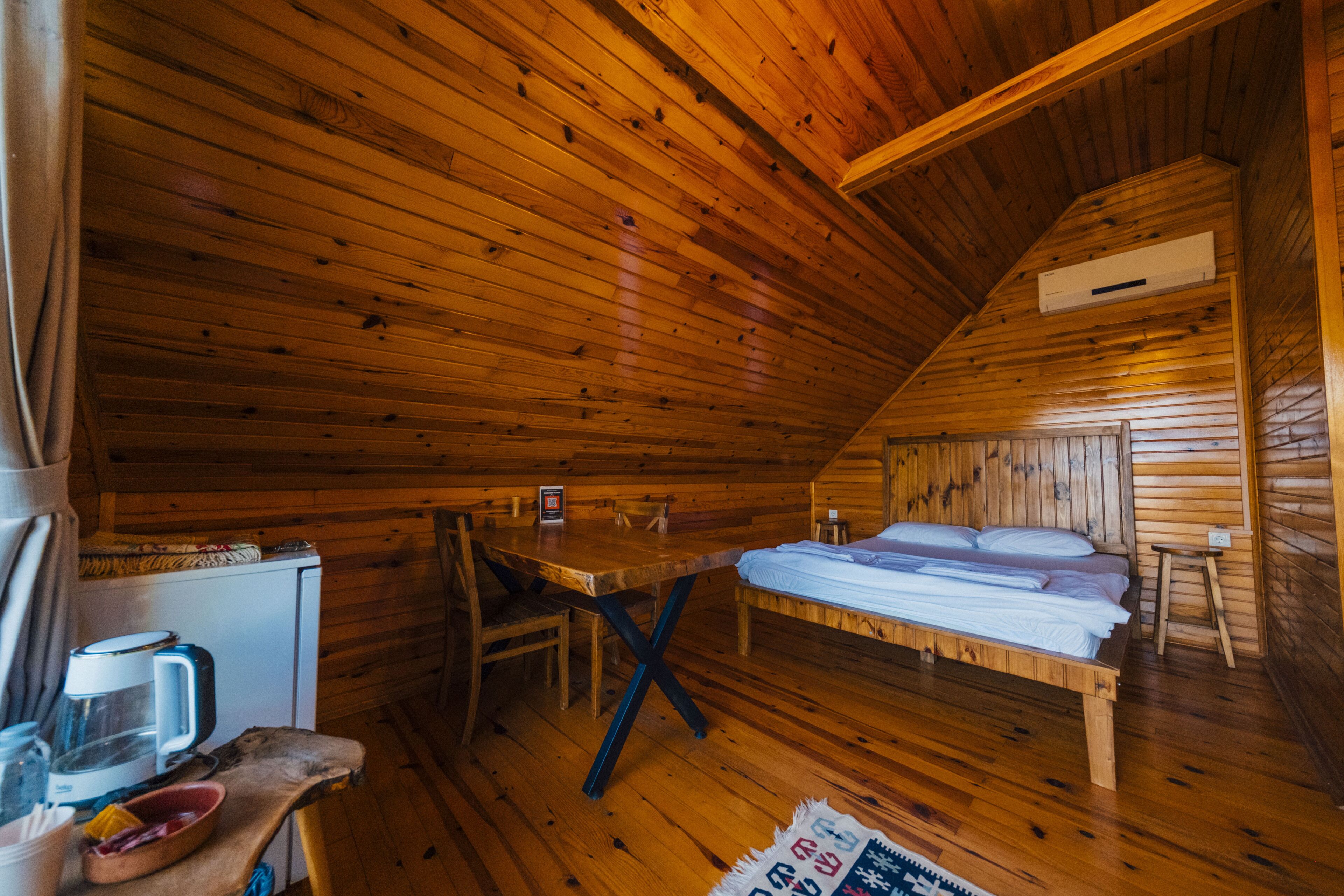 Uma cabana acolhedora com interior de madeira, uma cama, uma mesa e uma pequena cozinha.