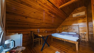 Uma cabana acolhedora com interior de madeira, uma cama, uma mesa e uma pequena cozinha.