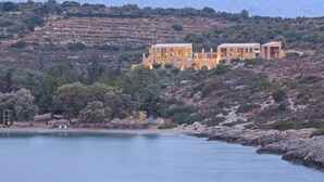Um imóvel costeiro com dois edifícios modernos, uma praia com guarda-sóis e uma encosta rochosa.