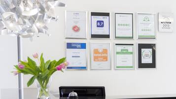 Uma parede exibindo diversos prêmios e certificados de um hotel, incluindo o prêmio de Vencedor TripAdvisor 2013 e o selo de Hotel com Melhor Avaliação HolidayCheck 2014.