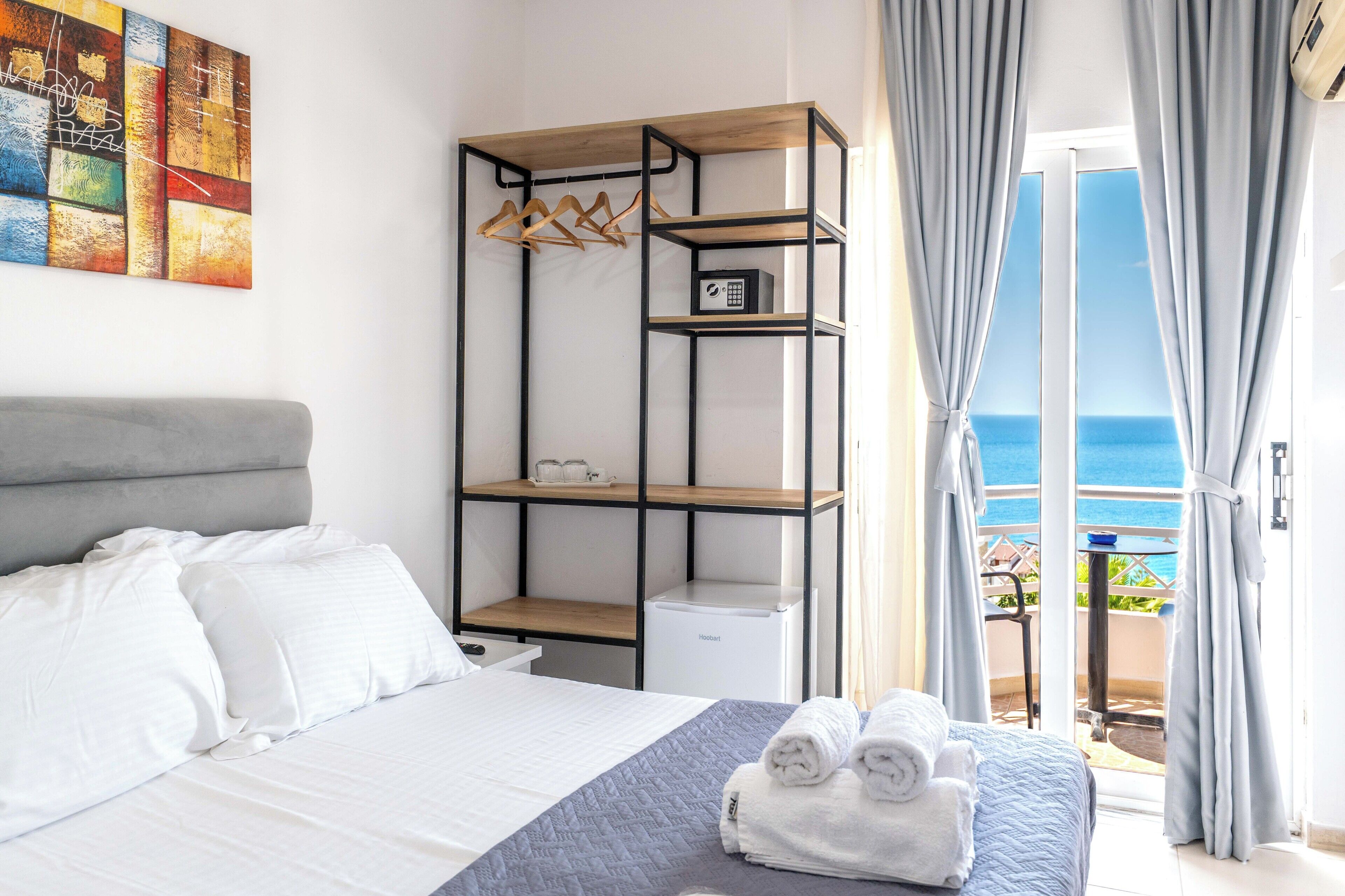 Quarto de hotel com cama, guarda-roupa, mini-frigorífico e vista para o mar.