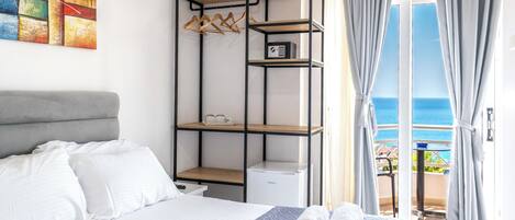 Quarto de hotel com cama, guarda-roupa, mini-frigorífico e vista para o mar.
