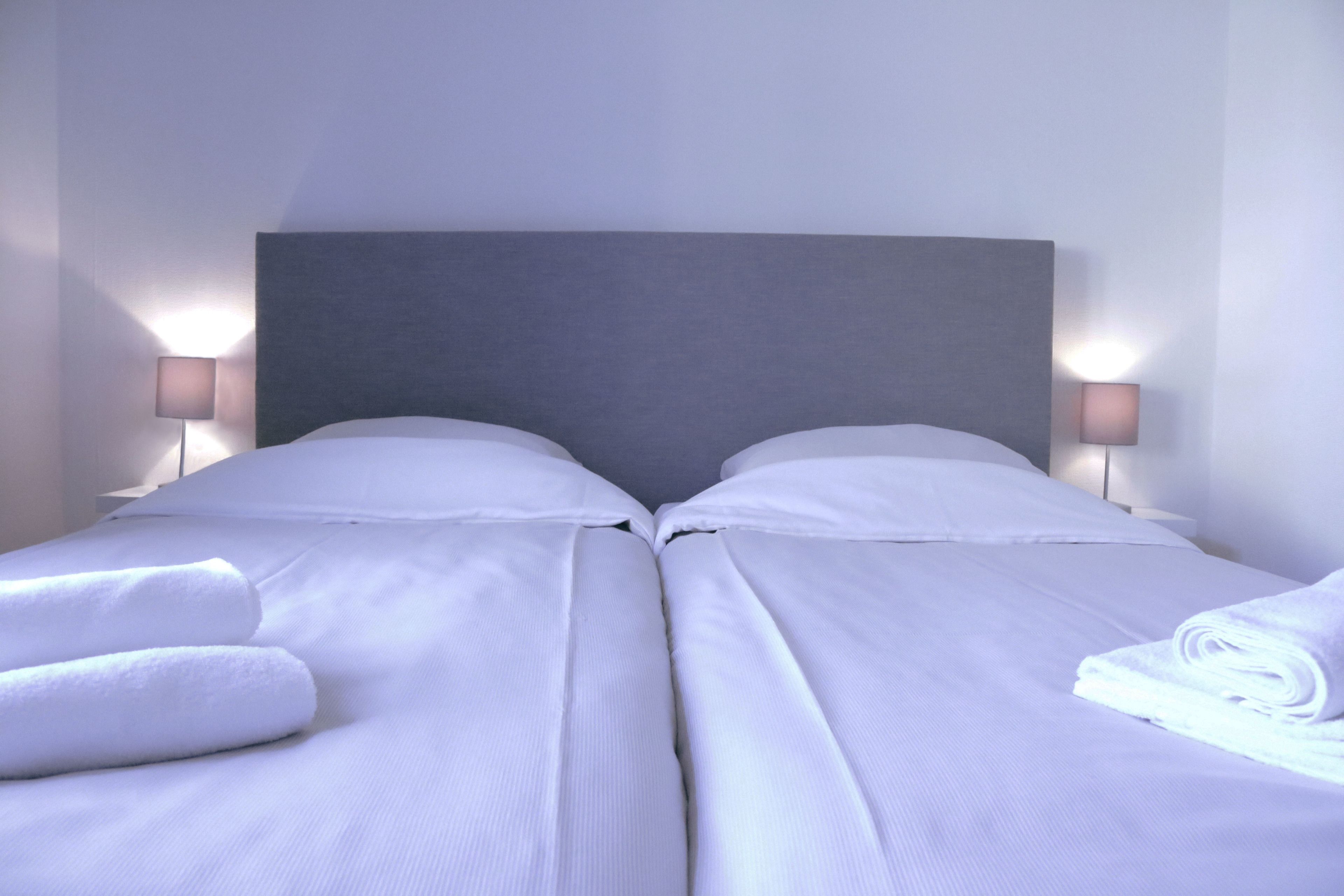 Uma cama de casal com lençóis brancos e duas luminárias de cabeceira.