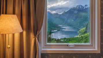 Quarto com janela que mostra uma paisagem montanhosa e um rio.