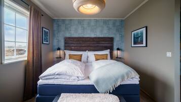 Quarto com cama grande, cabeceira de madeira, duas luminárias de cabeceira, janela com cortinas e vista para o exterior.