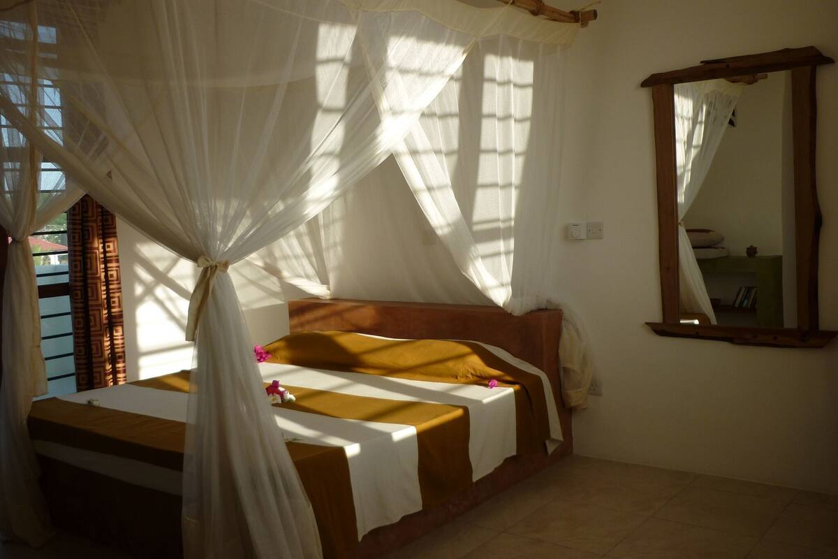 Quarto com cama sob um dossel, espelho na parede e janela com cortinas.