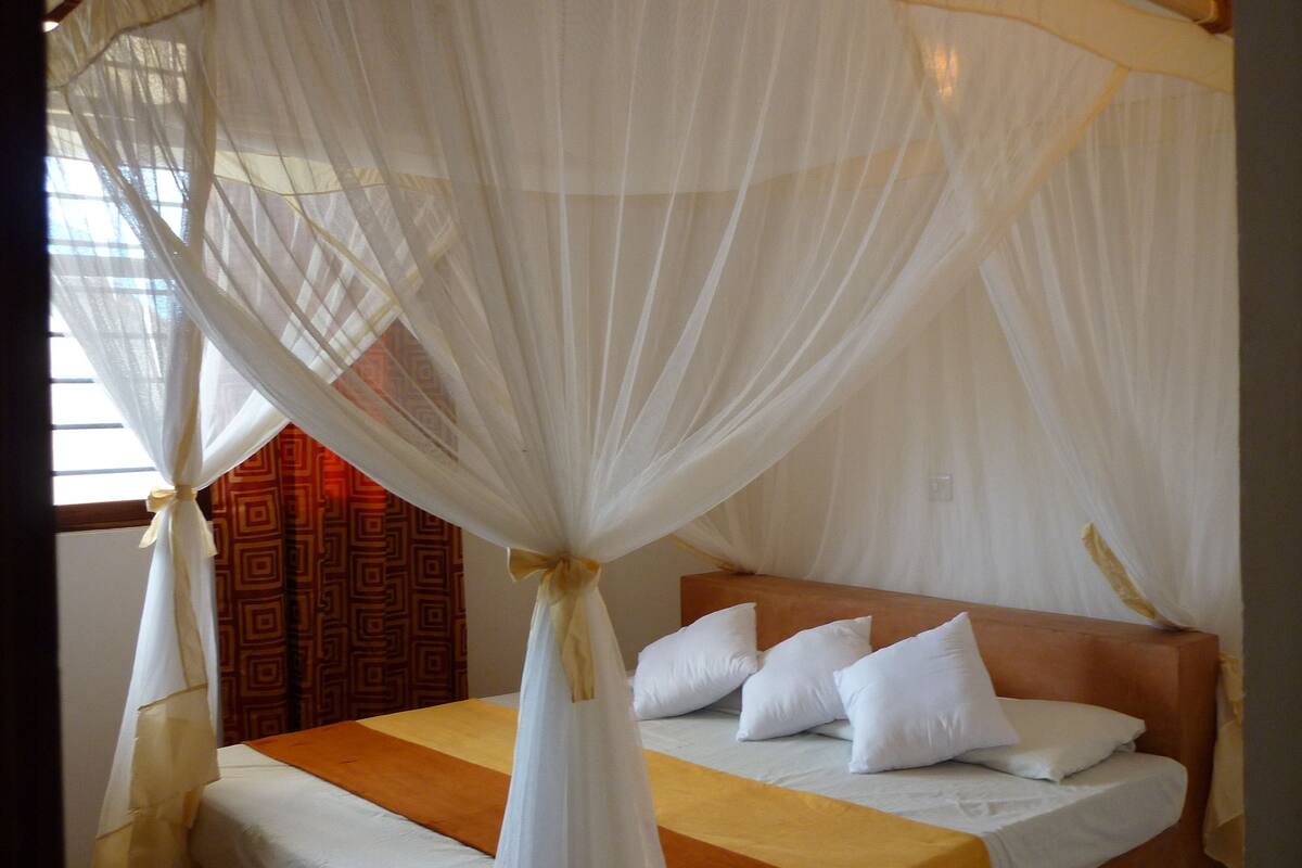 Quarto com cama sob um dossel, parede estampada e janela com cortinas.