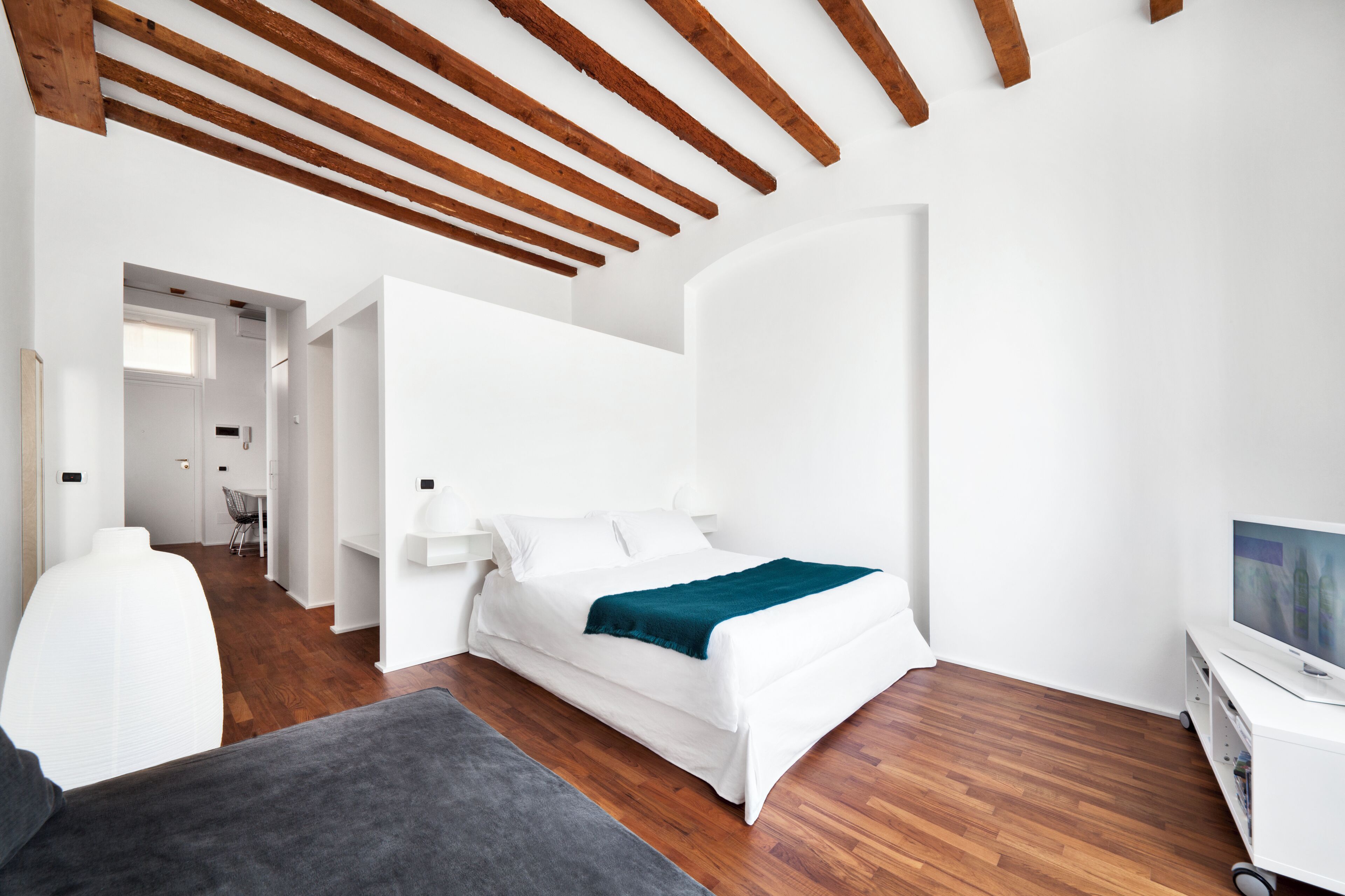 Um quarto moderno com uma cama, uma TV e teto de madeira.