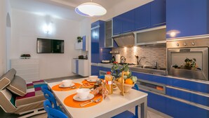 Cozinha moderna com armários azuis, forno de aço inoxidável e área de jantar com mesa posta para dois.