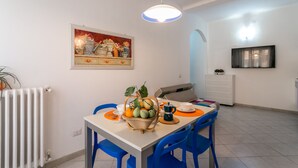 Uma área de refeições com uma mesa posta para dois, uma cesta de frutas e um quadro na parede.