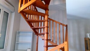Uma escada espiral de madeira em um quarto com paredes brancas e uma janela com persianas.