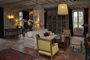 Uma sala de estar acolhedora com um sofá branco, uma cadeira de madeira, uma mesinha com uma vela e vista para o exterior pela janela.